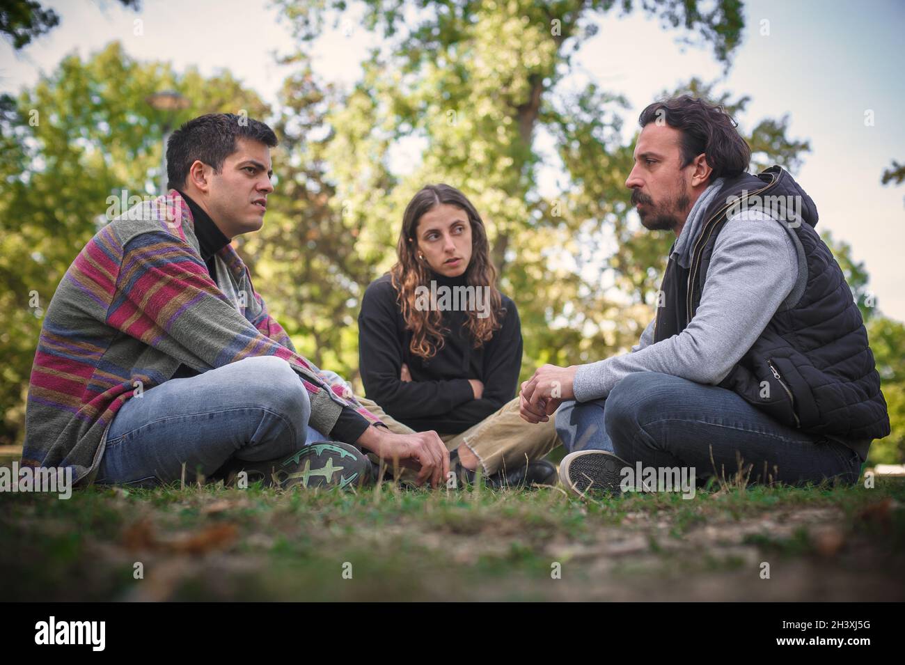 Three worried friends, two men and a girl, sit together on the ground ...