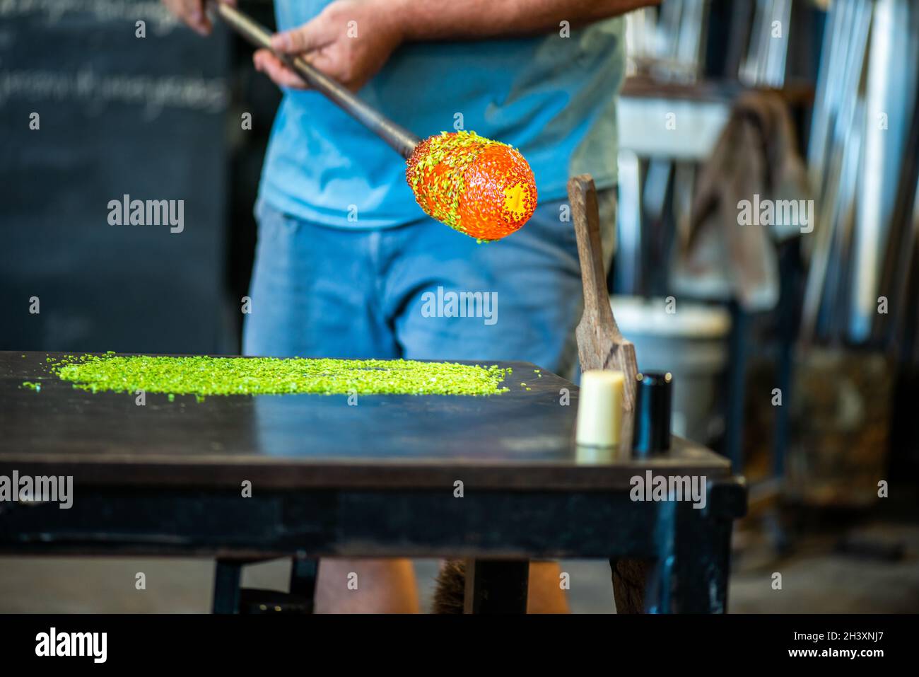 a worker is in the process of creating a glass vase and is rolling ...