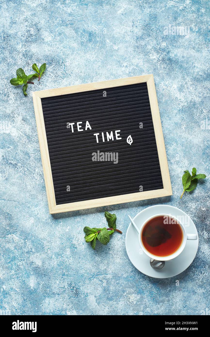 Tea time. Black letter board with text on blue table with glass cup of ...
