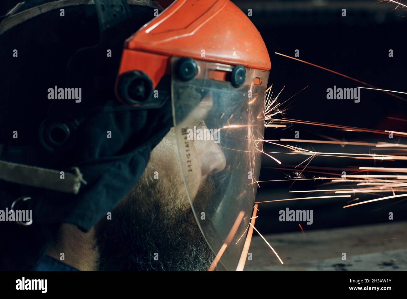 Man worker in transparent protective mask works on metal with circular ...