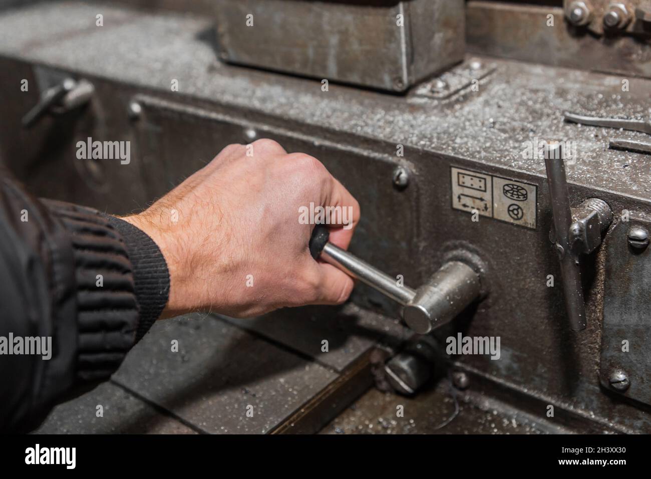 The hand of a man in a black work jumpsuit controls a milling machine ...
