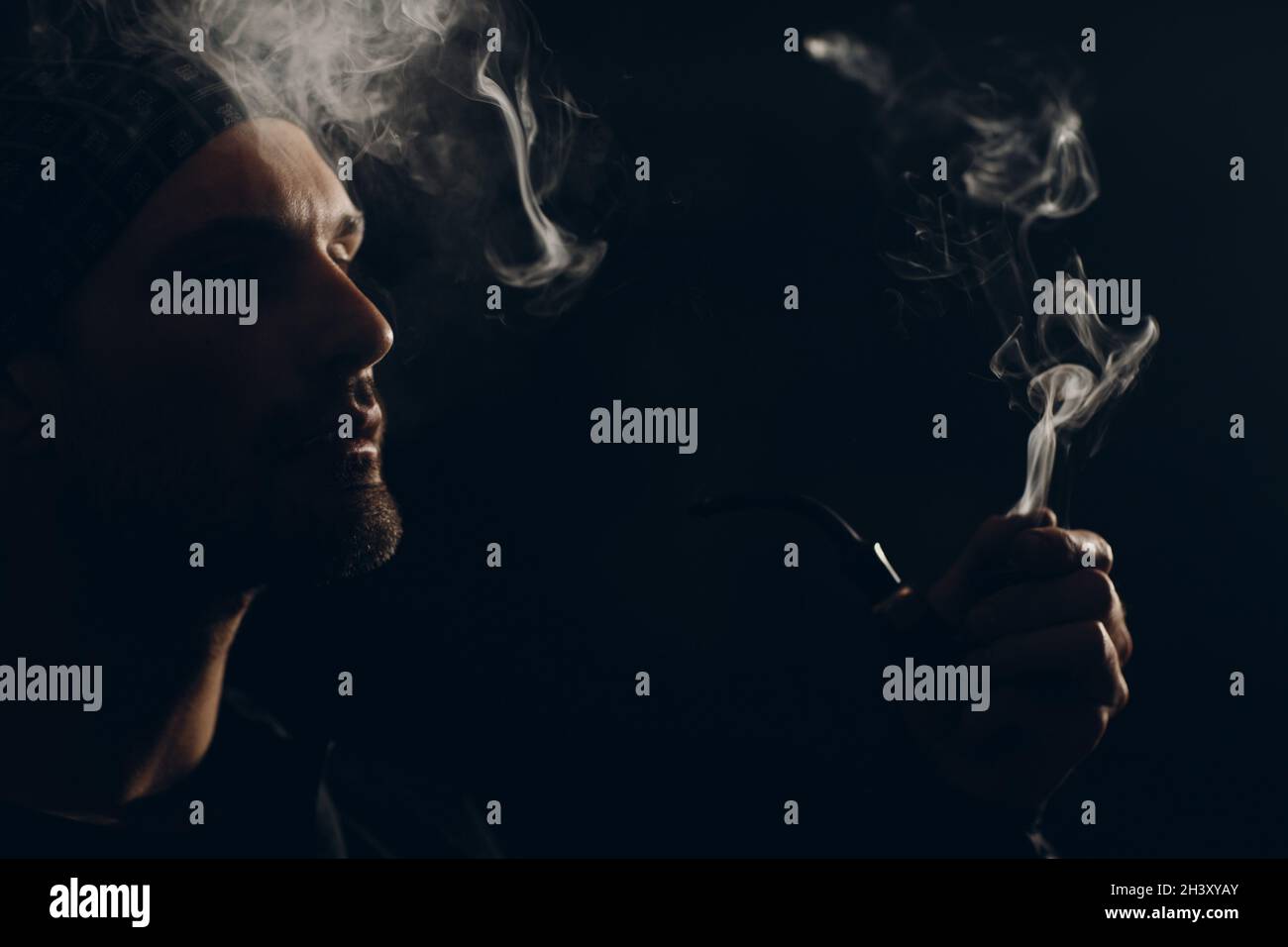 Man smoking a pipe on dark background. Back lit profile portrait Stock ...