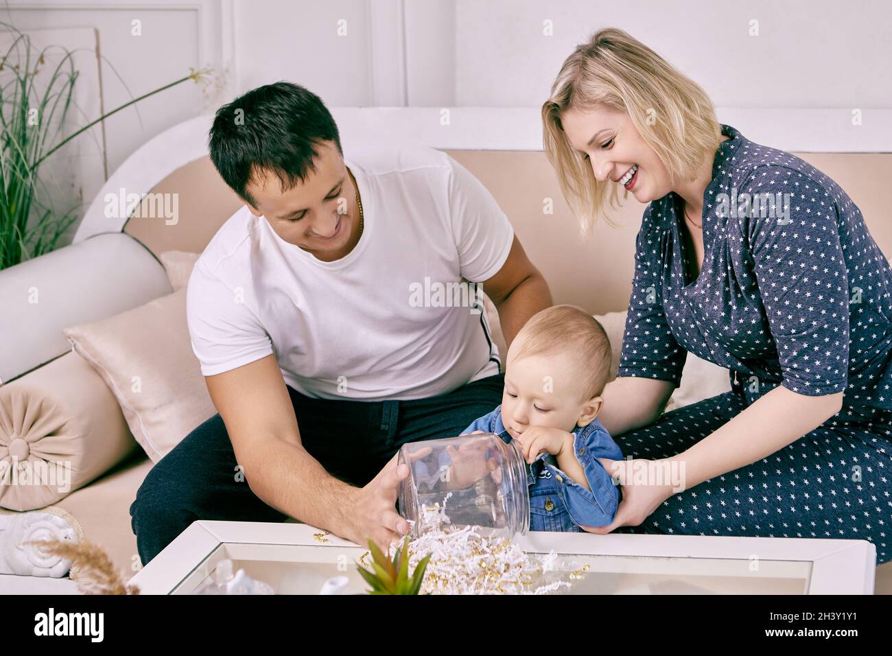 Toddler and smiling parents sit on sofa in living room Stock Photo - Alamy