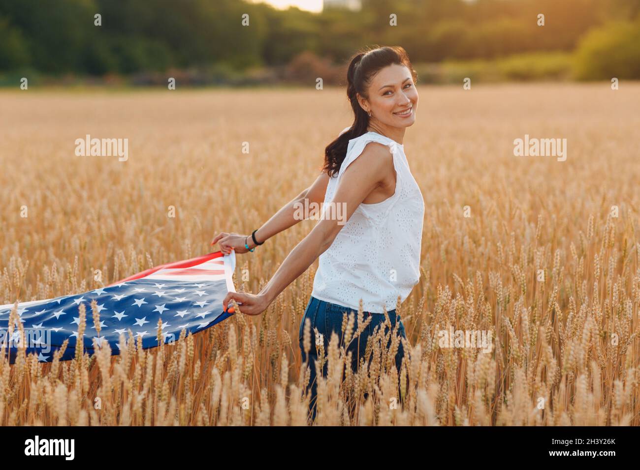 Woman with American flag in wheat field at sunset. 4th of July ...