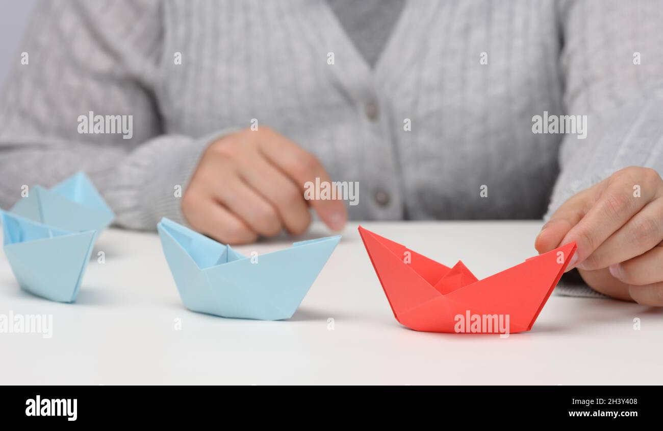 Group of blue paper boats follows a red boat in front of a white ...