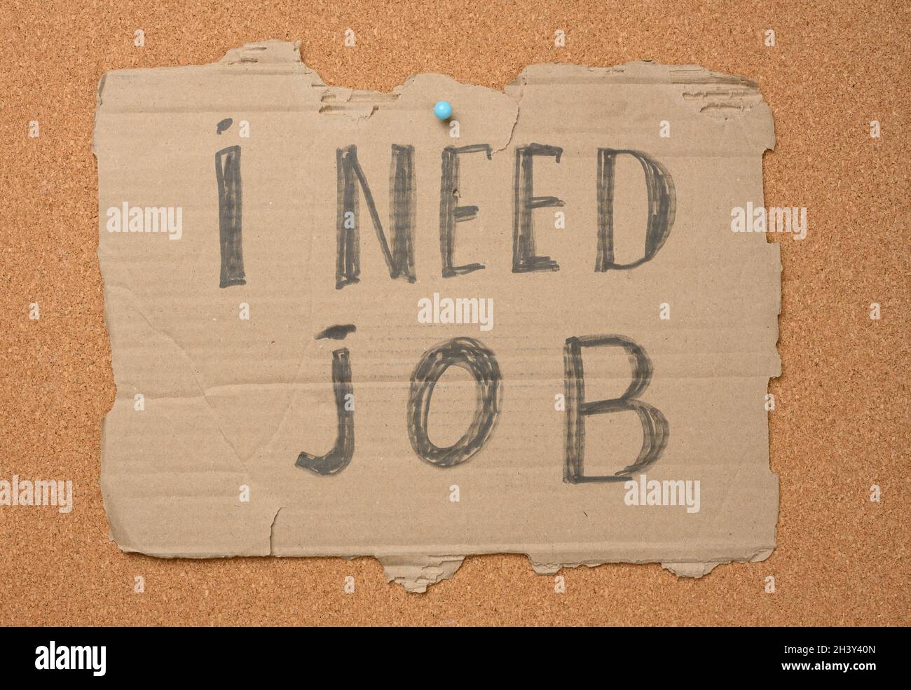 A torn brown piece of cardboard with a lettering i need job attached to ...
