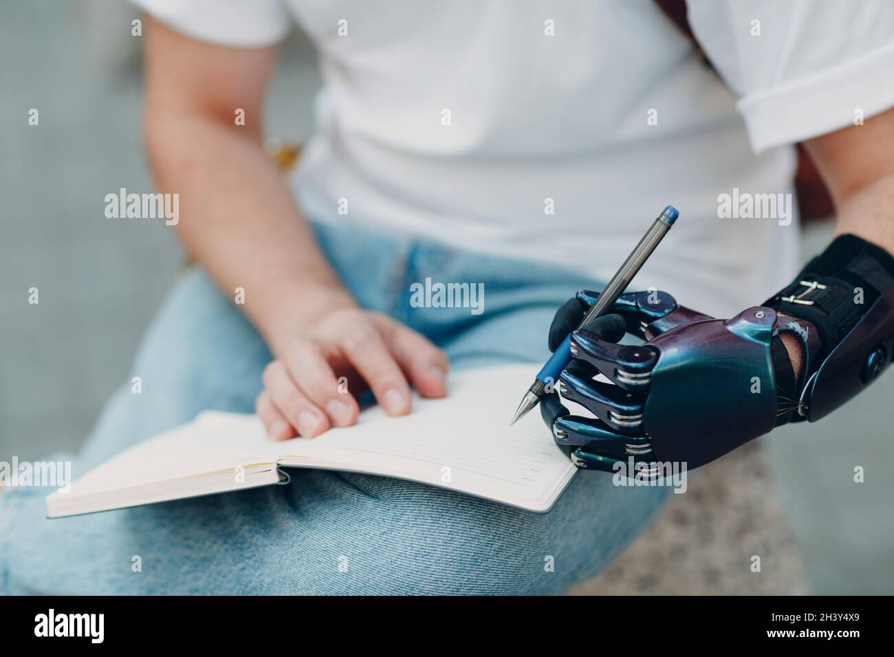Young disabled man writes in notebook with pen in artificial prosthetic ...