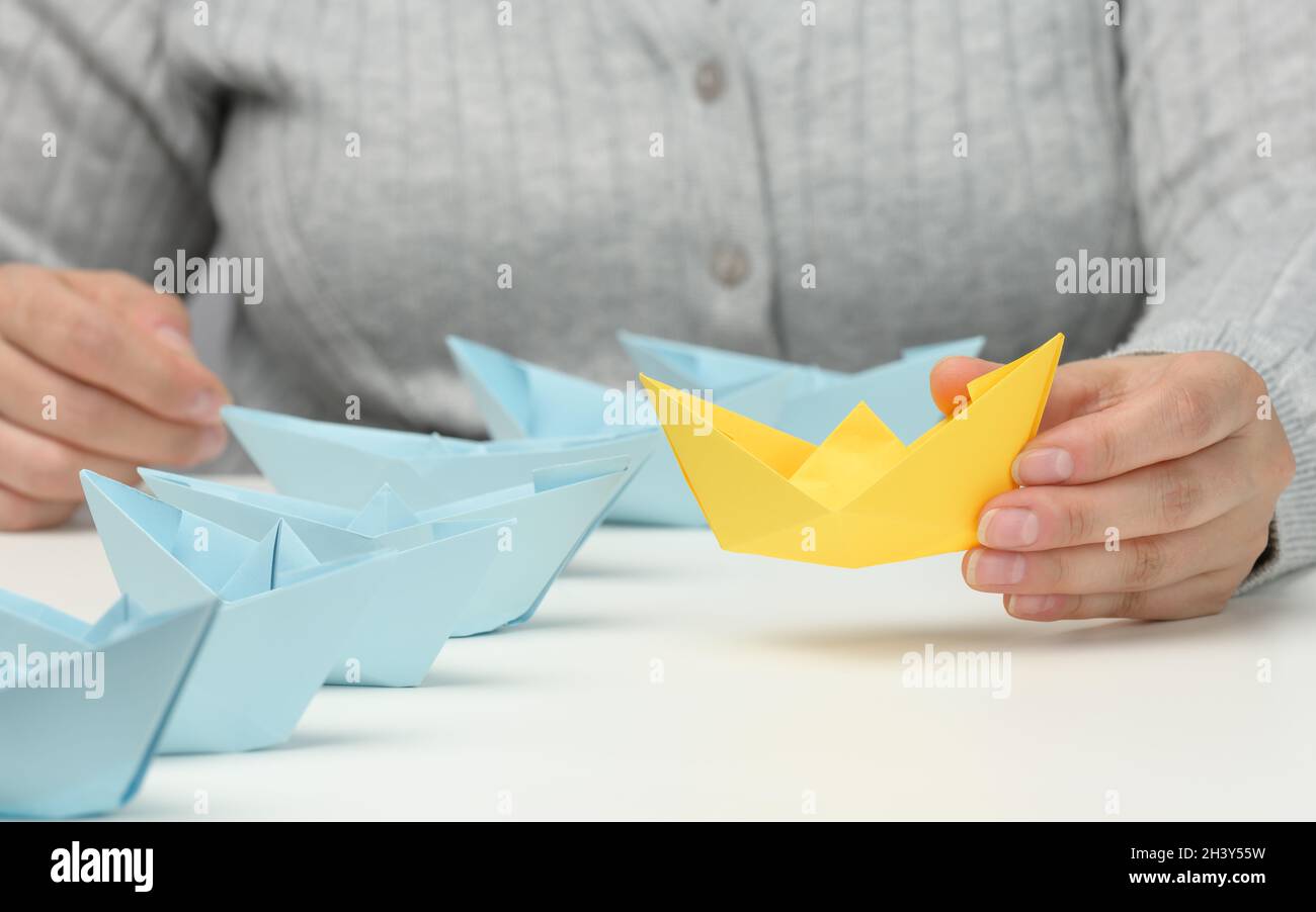 Group of blue paper boats follows a yellow boat in front of a white ...