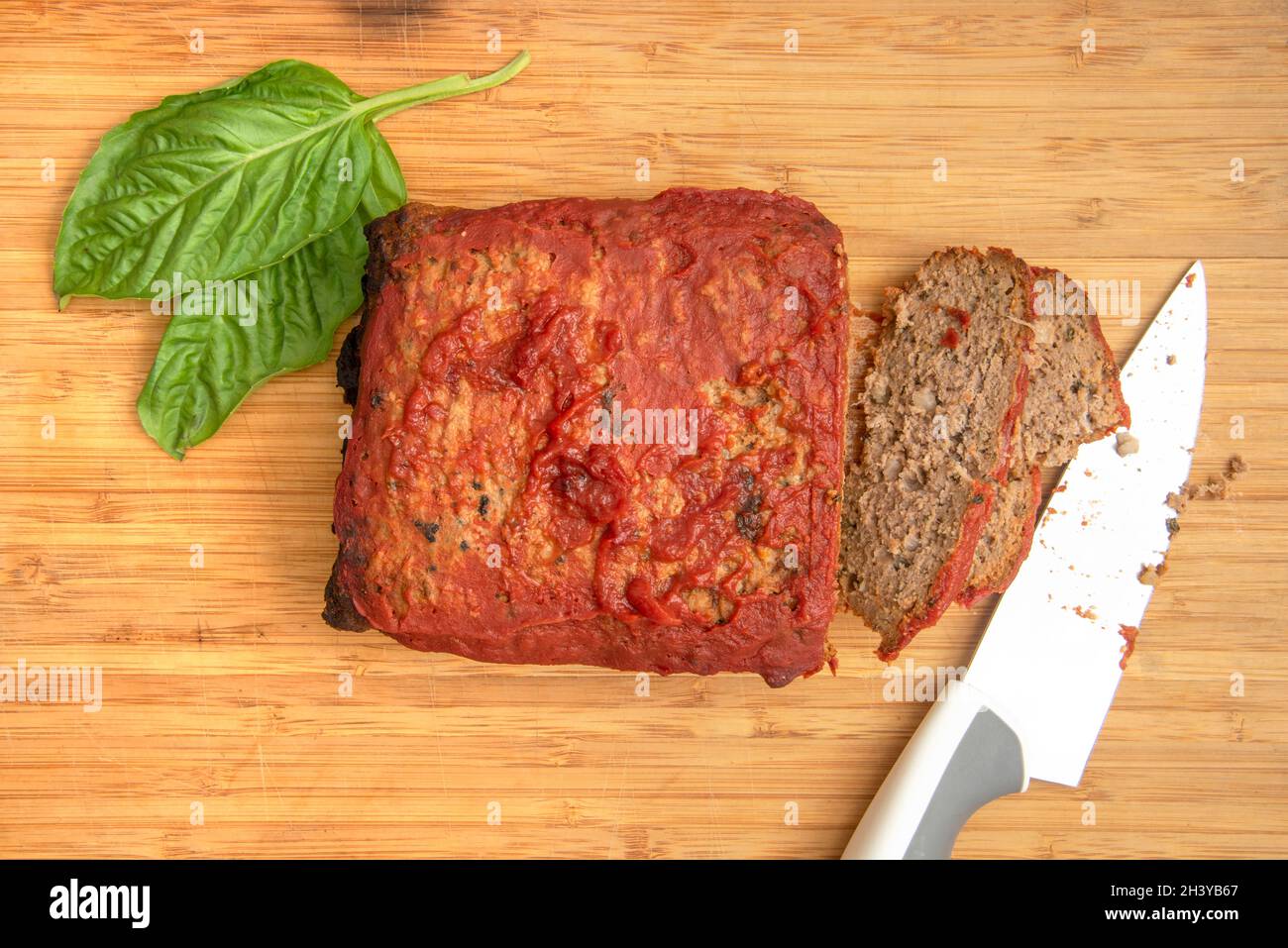 A fresh baked sliced meatloaf on a cutting board with tomato sauce ...