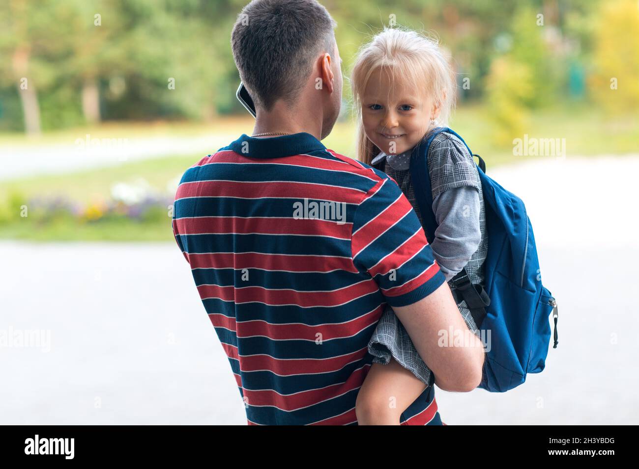 Rear view of father walking back to school with his daughter carrying ...