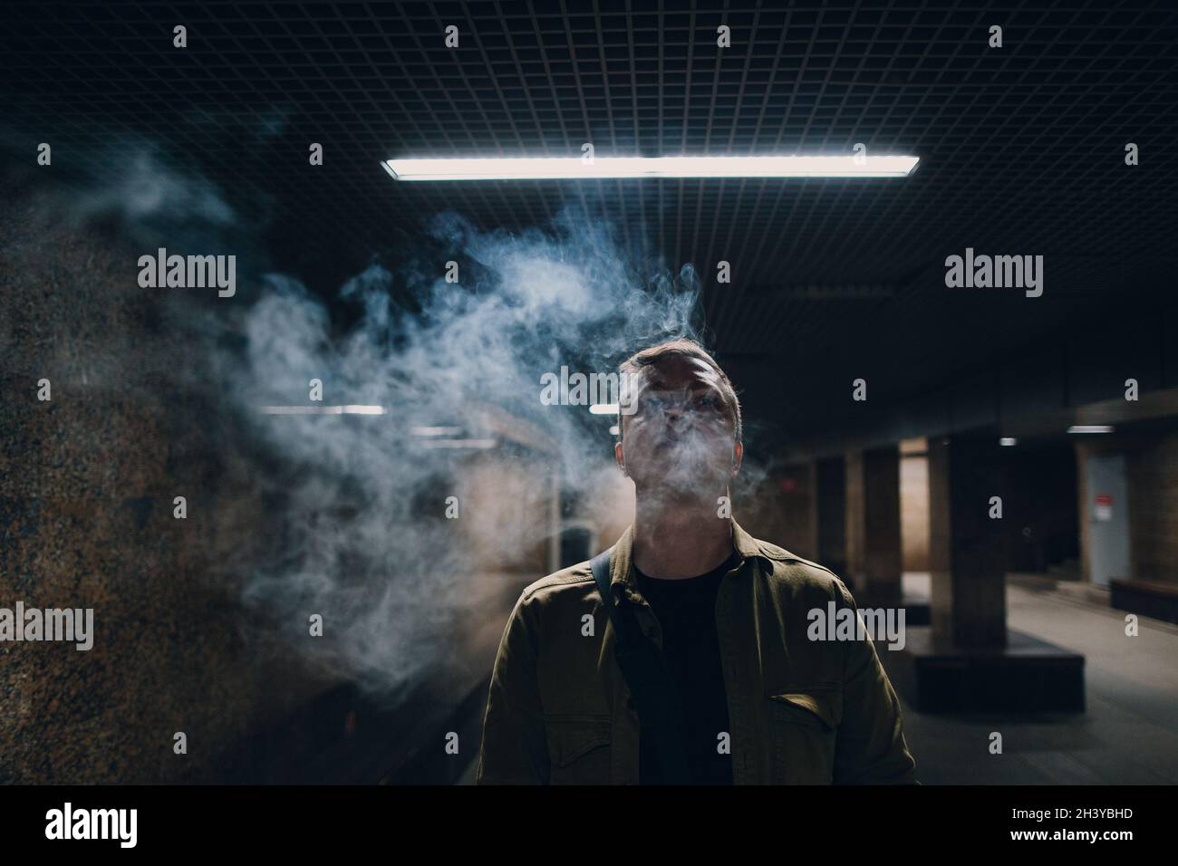 Portrait of young caucasian man smoking e-cigarette in dark with line ...