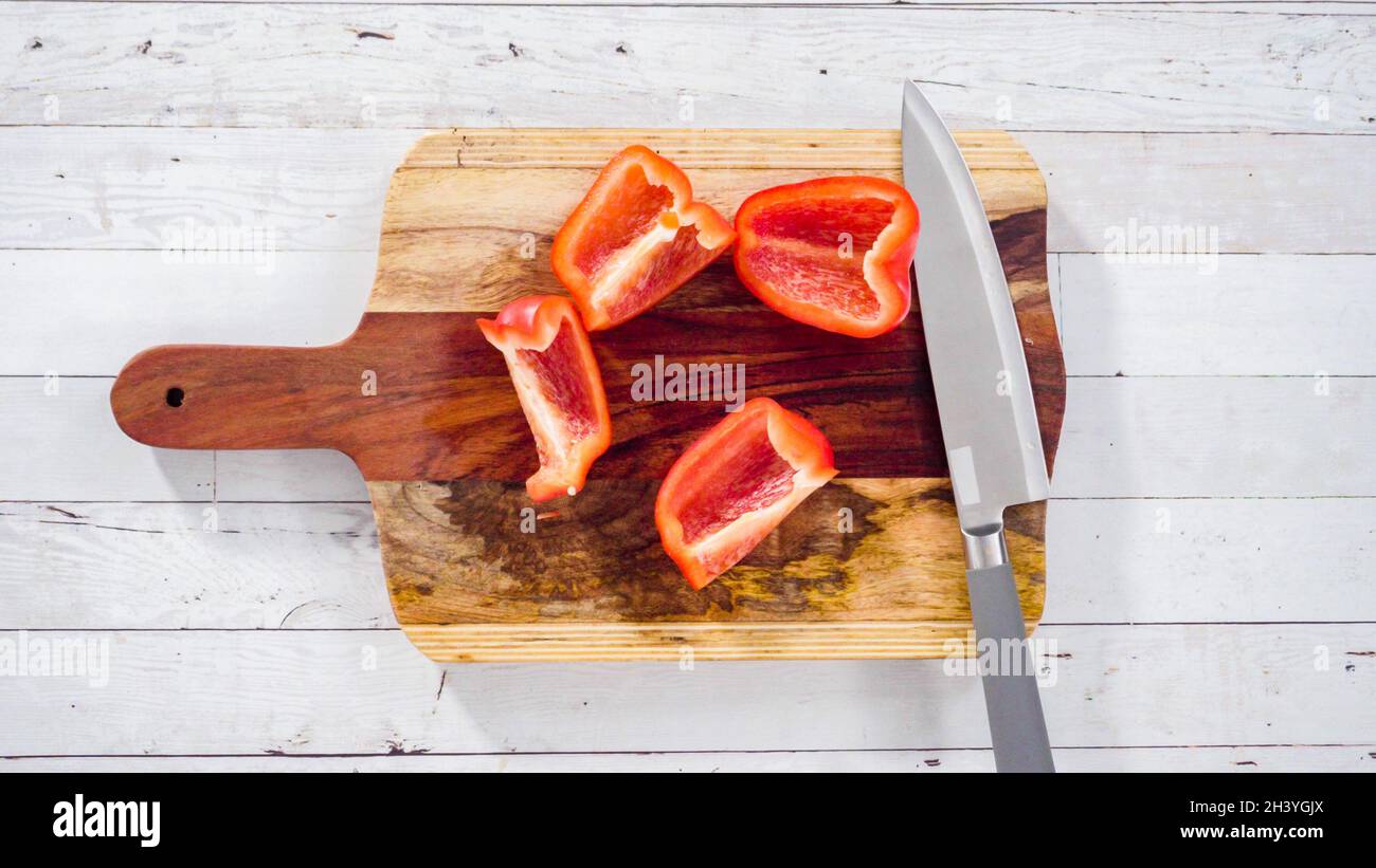 Flat lay. Mincing organic red bell peppers on a wood cutting board ...