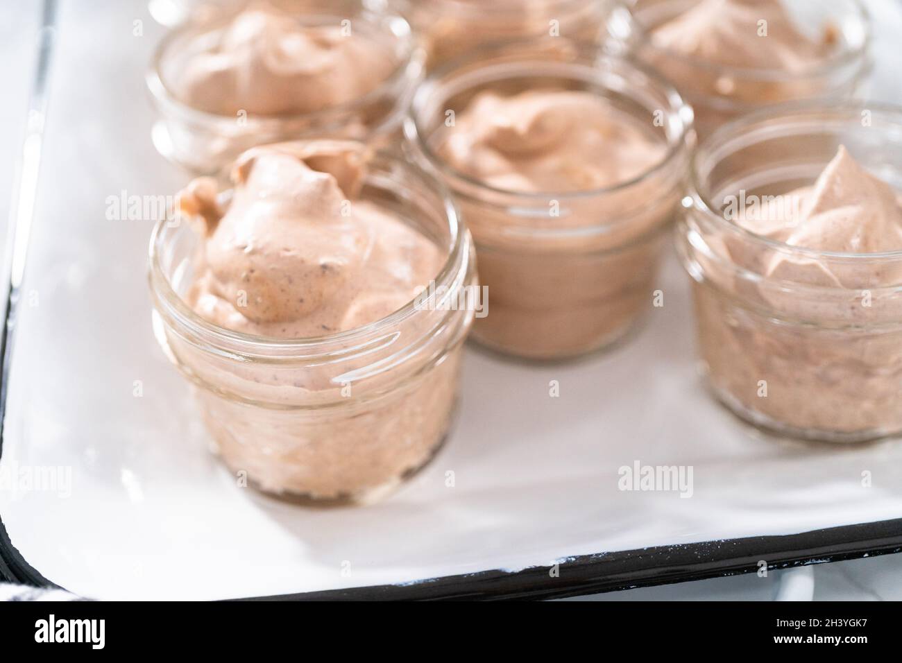 Scooping mixture into the small glass jars to make homemade chocolate ...
