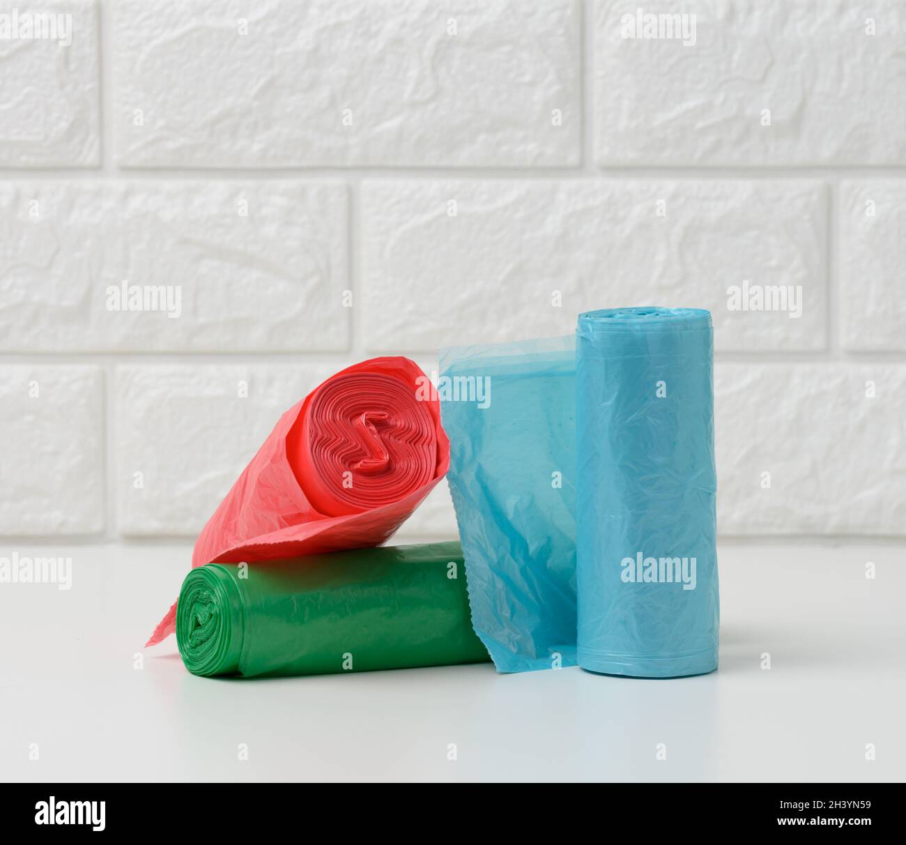 Stack of disposable plastic trash can bags on white table, white brick ...