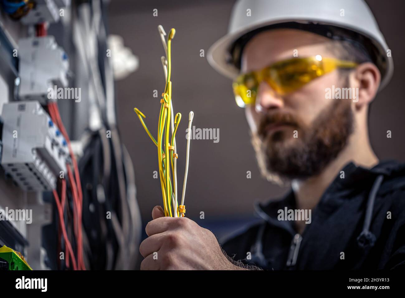 A male electrician works in a switchboard with an electrical connecting ...