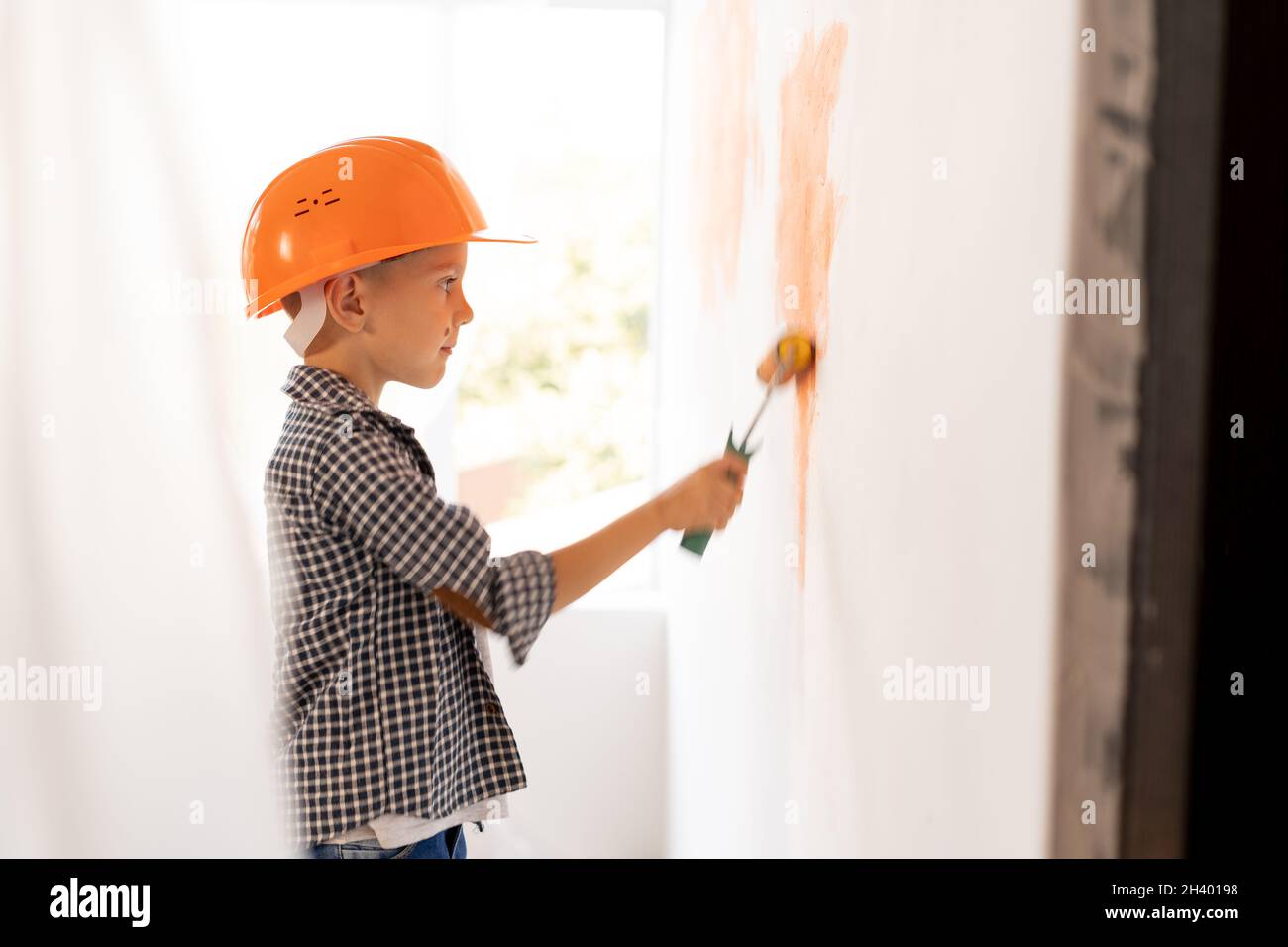 Caucasian child boy paints the wall with paint roller indoors doing ...