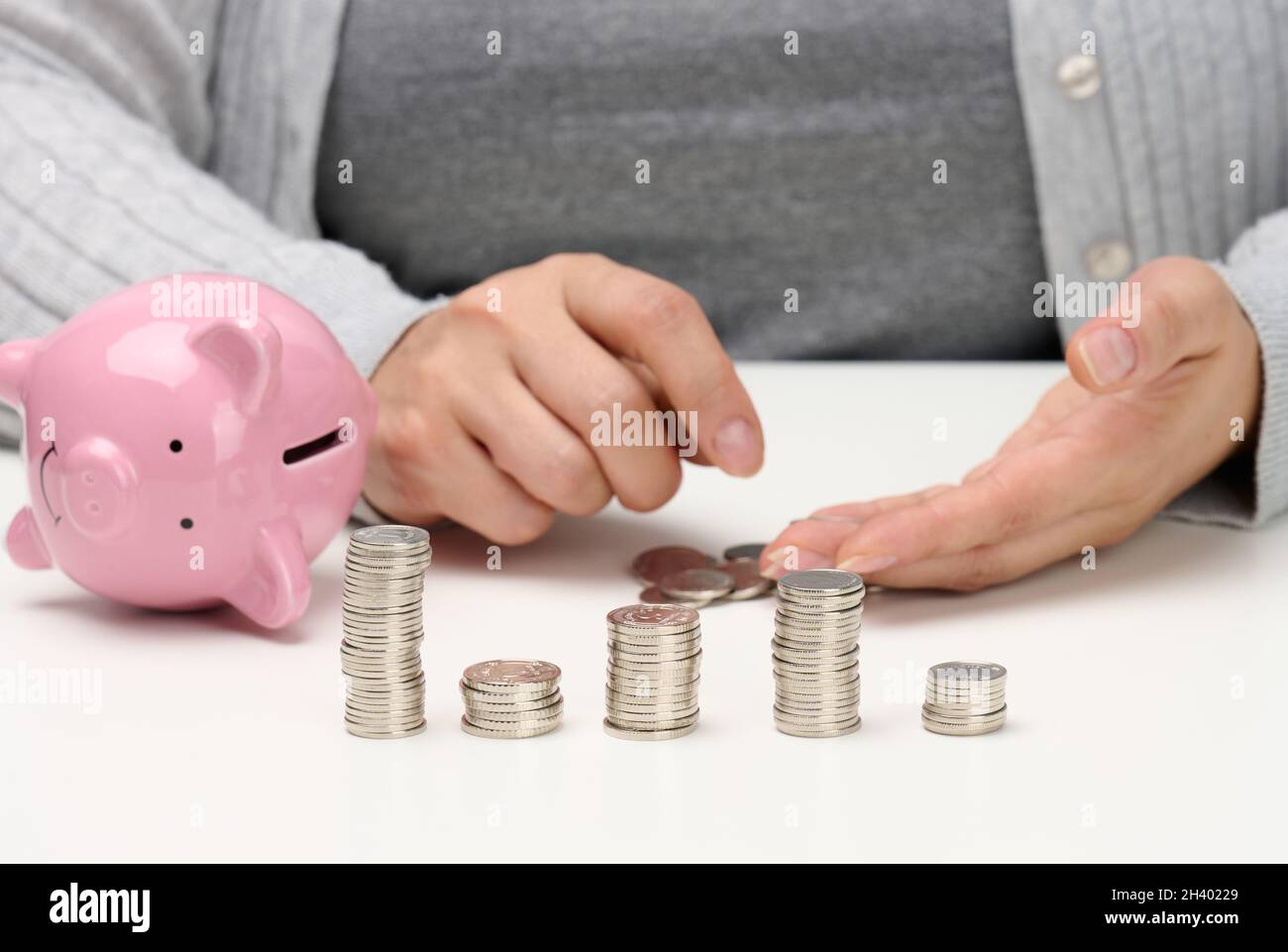 Stack of metal coins and a ceramic pink piggy bank. Man counting money ...