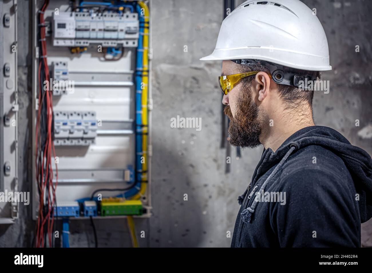 A male electrician works in a switchboard with an electrical connecting ...