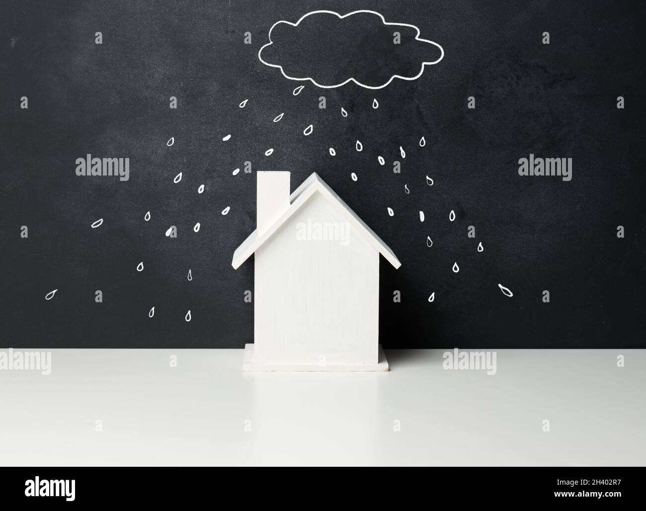 Wooden house and a drawn cloud with rain with white chalk on a black ...