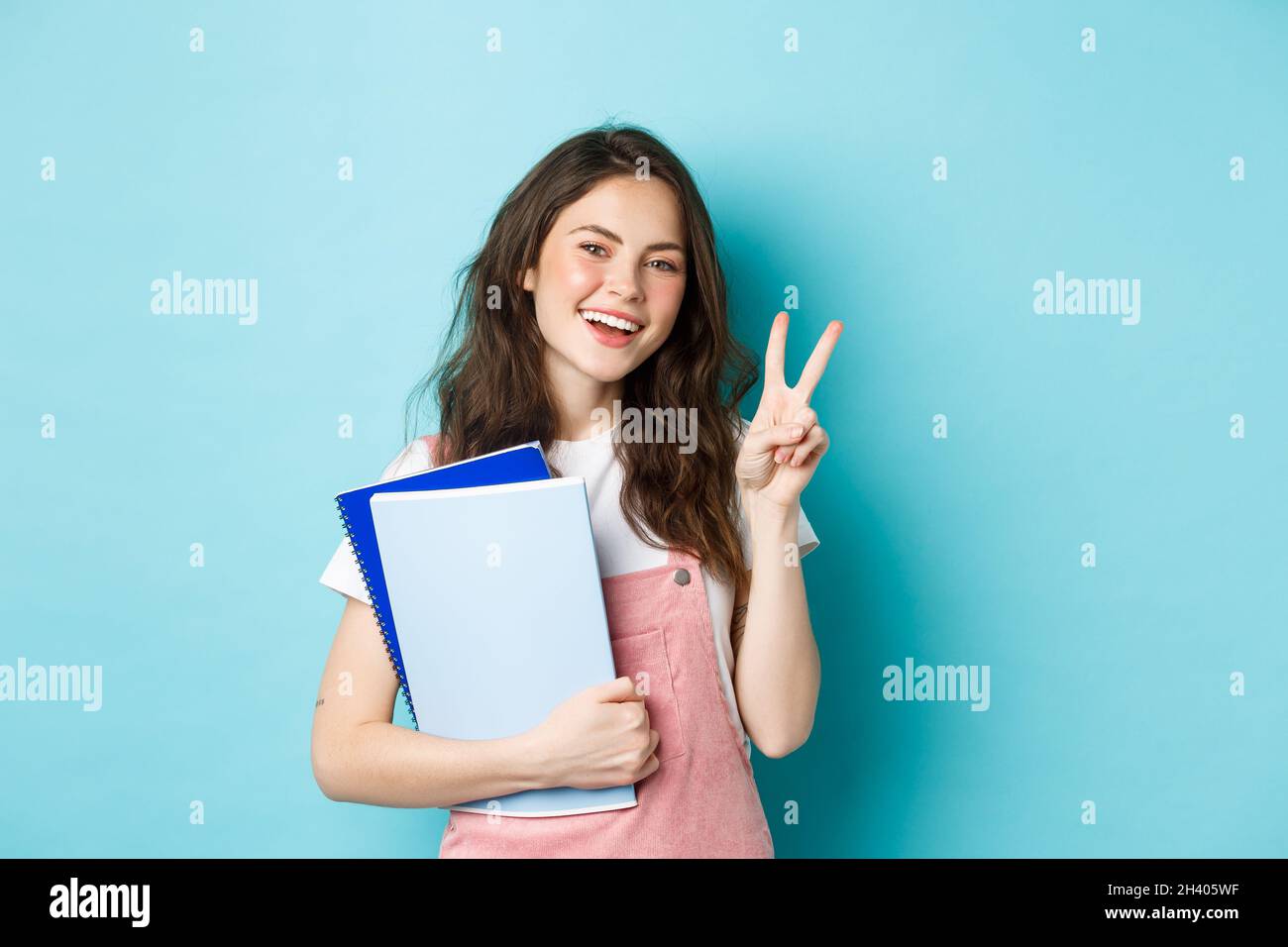Beautiful female student showing v-sign and smiling happy, holding ...