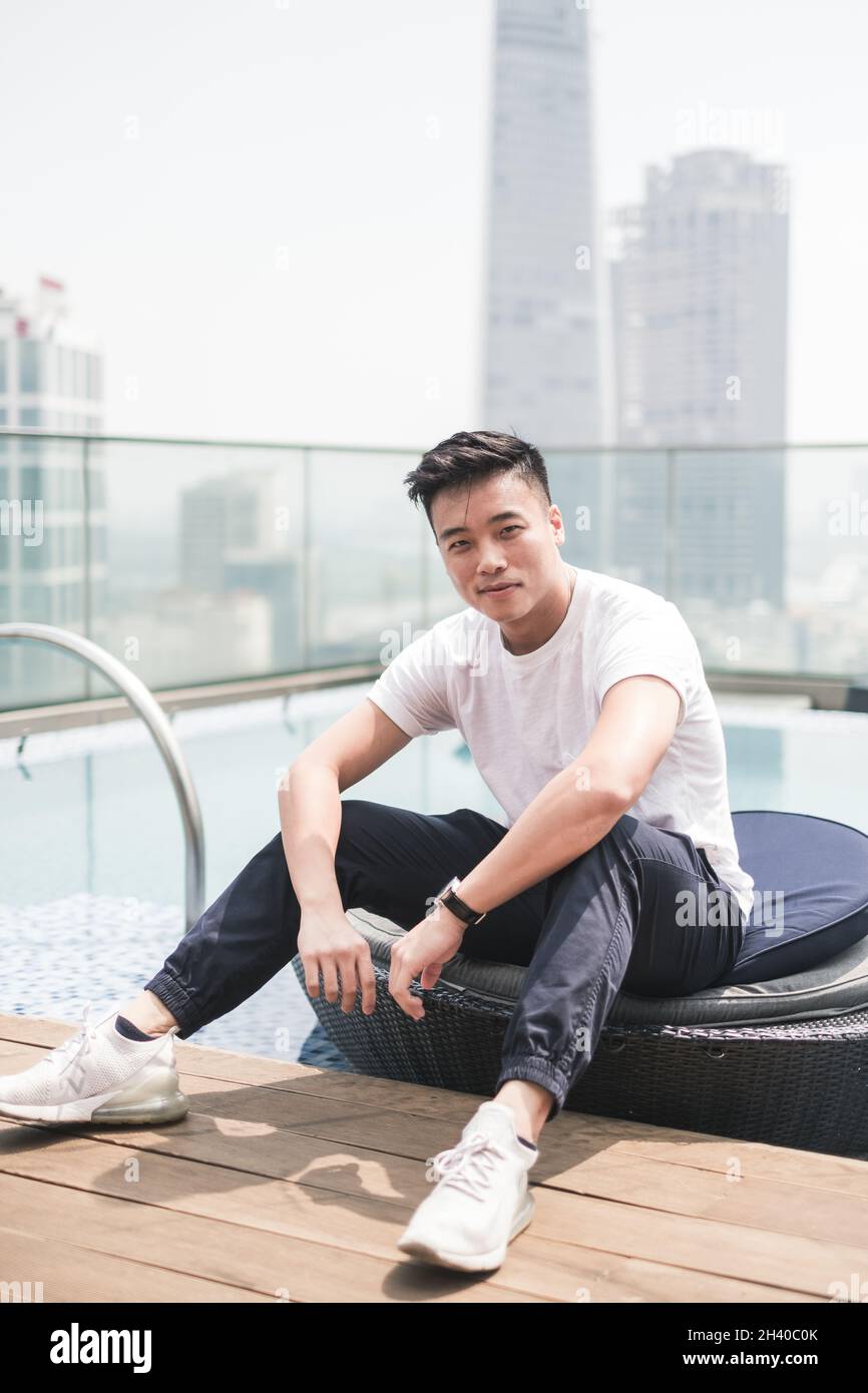 Handsome young Asian man sitting on the rooftop near the swimming pool ...