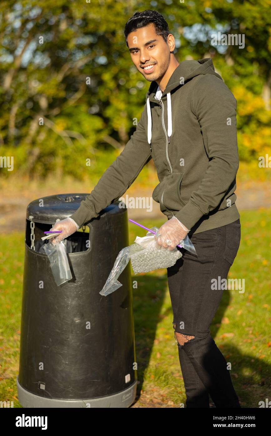Smiling young man putting plastic in garbage bin at park Stock Photo ...