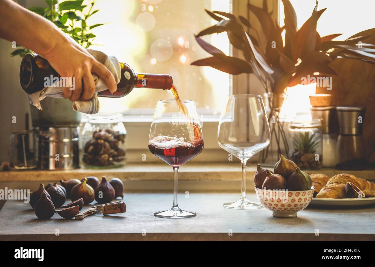 Hand pouring red wine from bottle in two wine glasses on kitchen table ...