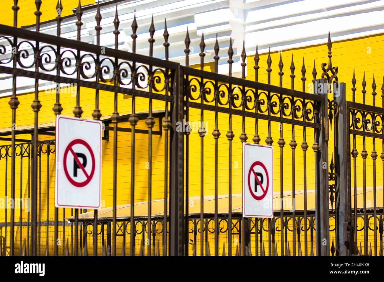 No Parking Sign on black metal wrought iron fence against yellow brick ...