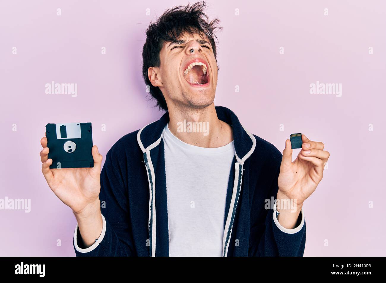 Handsome hipster young man holding floppy disk and sdxc card angry and ...