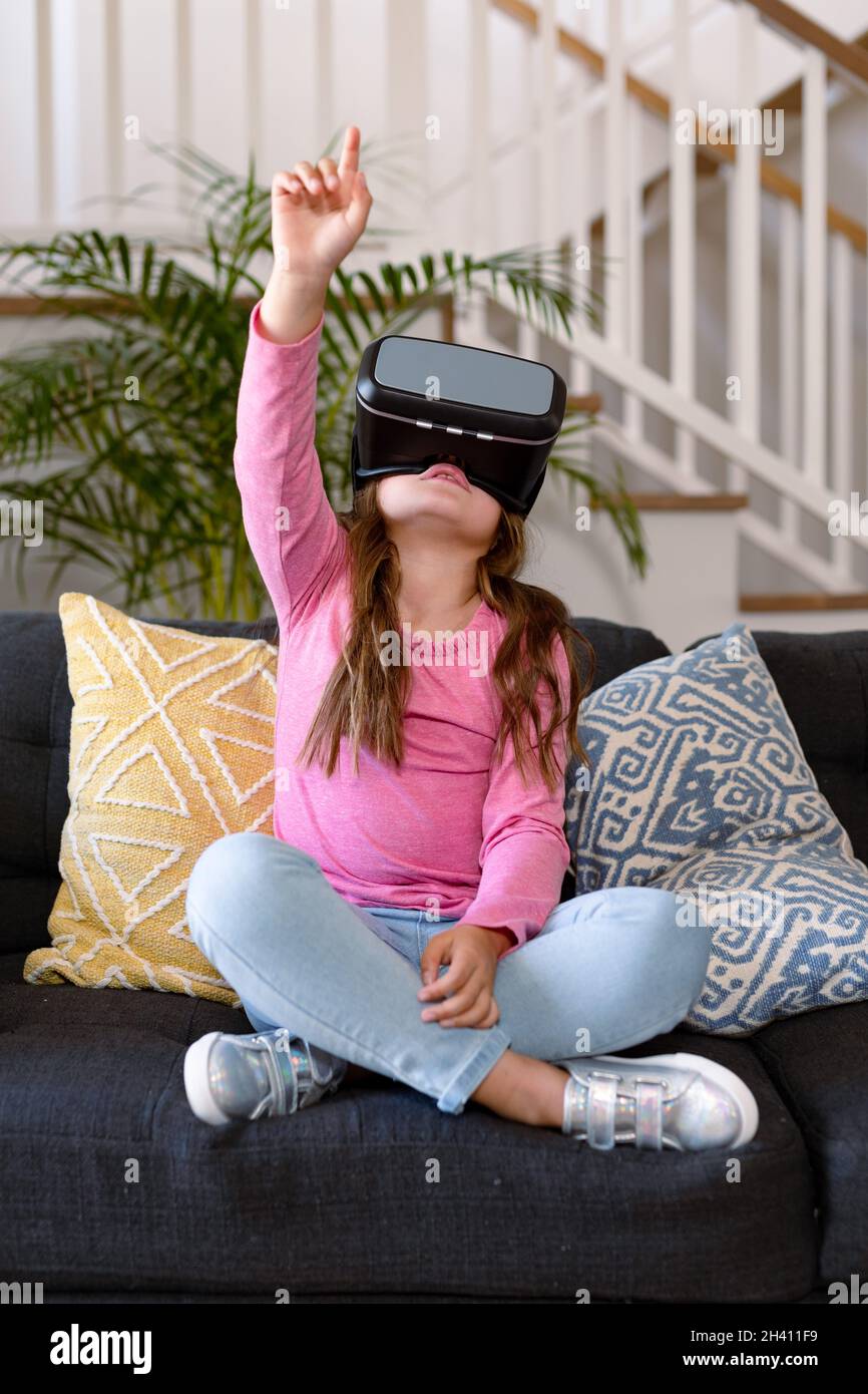 Happy caucasian girl sitting on sofa, wearing vr headset, having fun ...