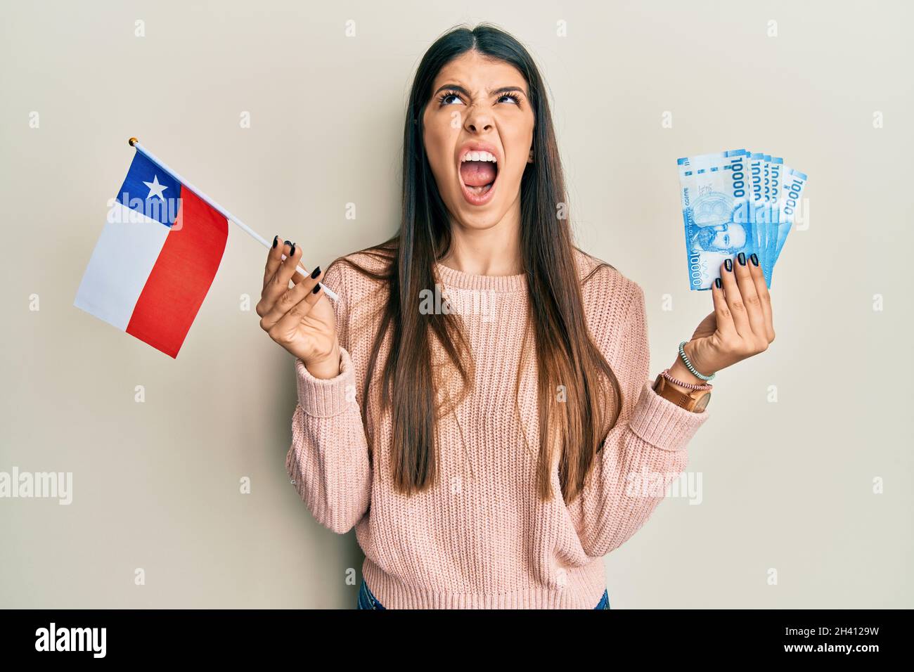 Young hispanic woman holding chile flag and chilean pesos banknotes ...