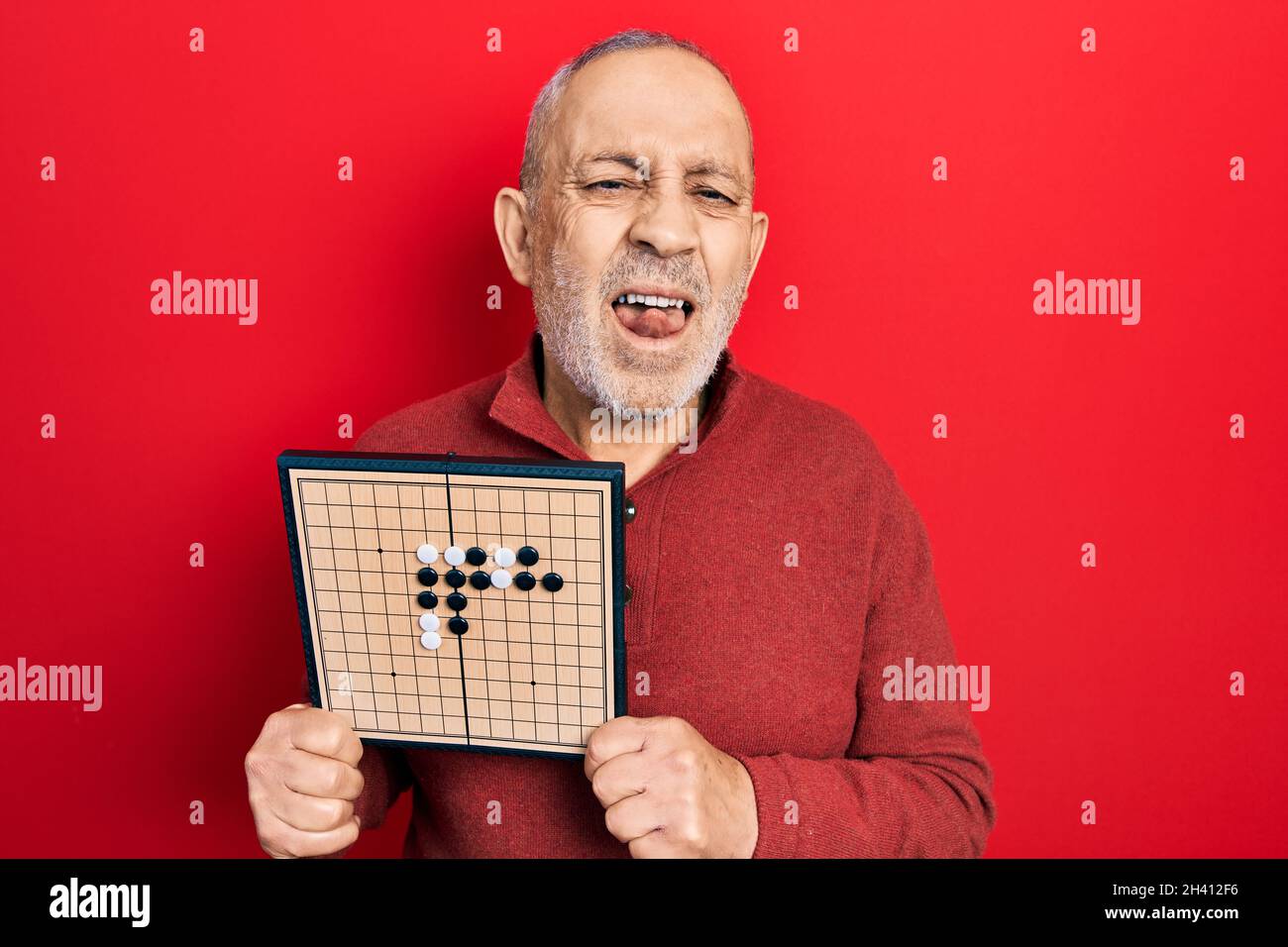 Handsome mature man holding asian go game board sticking tongue out ...