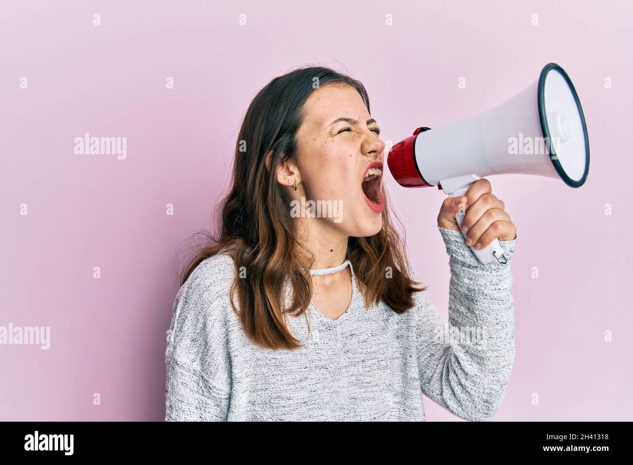 Young brunette woman shouting and screaming through megaphone over pink ...