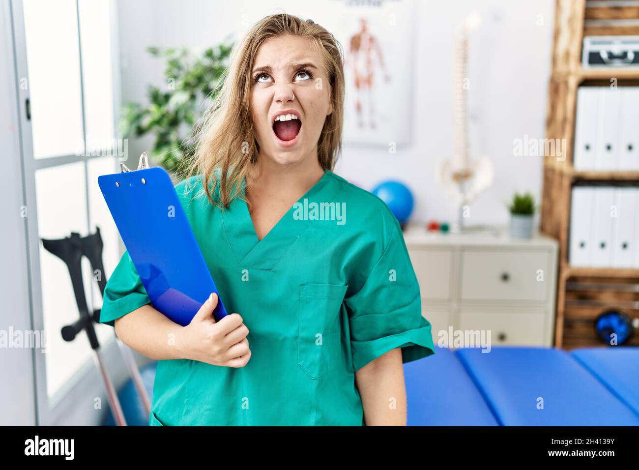 Young caucasian woman working at pain recovery clinic angry and mad ...