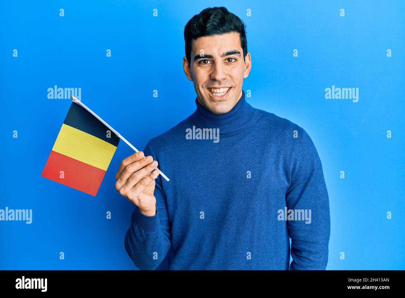 Handsome hispanic man holding belgium flag looking positive and happy ...