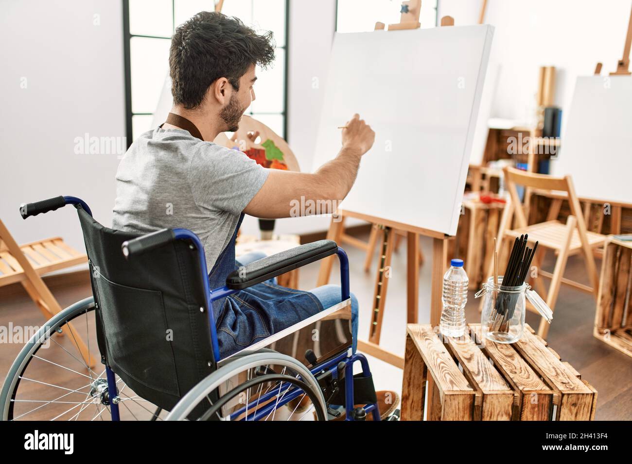 Young hispanic artist disabled man on back view painting at art studio ...