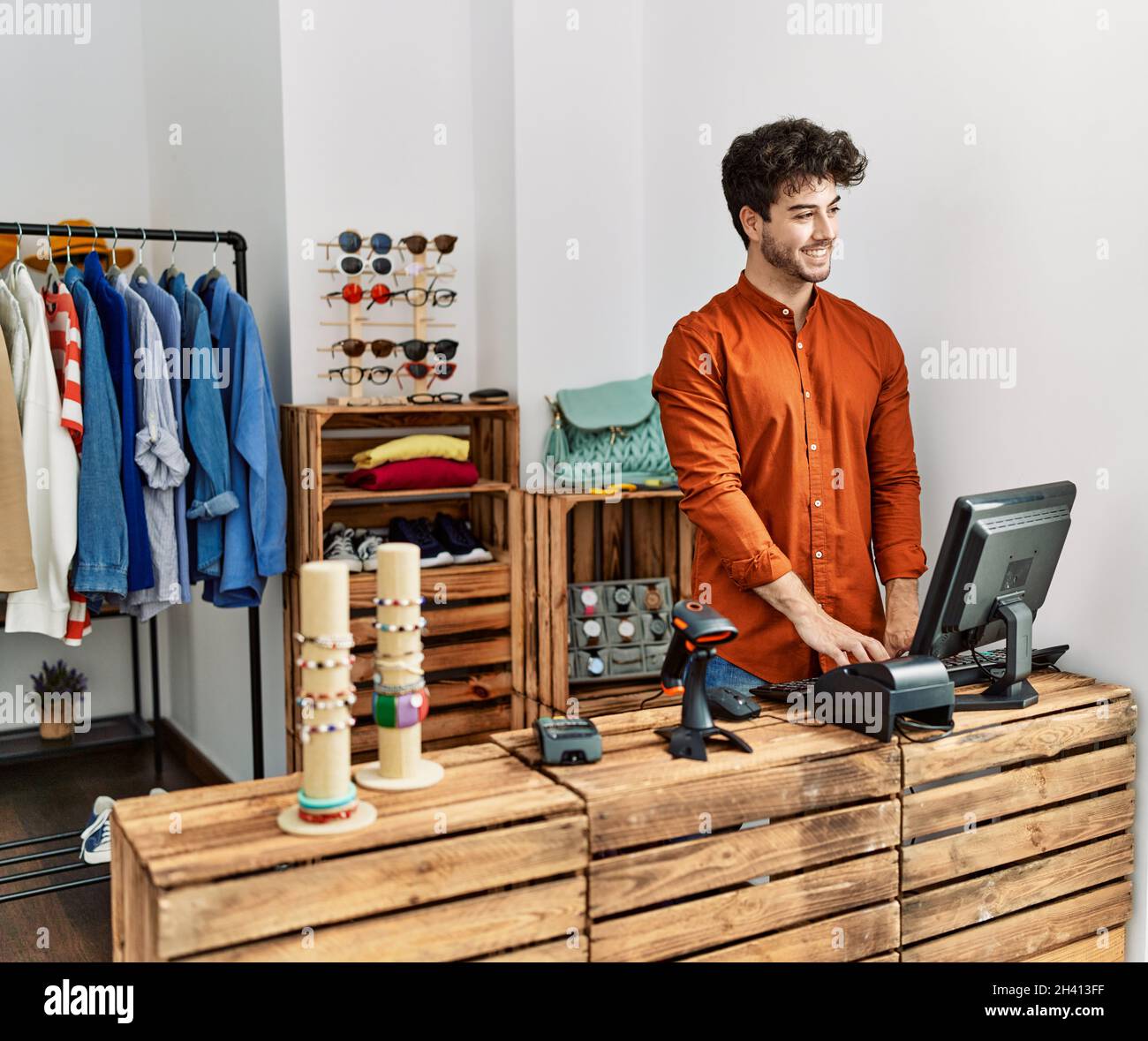 Young hispanic shopkeeper man smiling happy working at clothing store ...