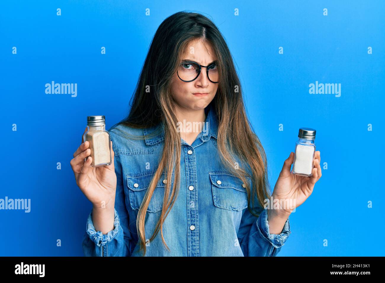 Young caucasian woman holding salt shaker skeptic and nervous, frowning ...