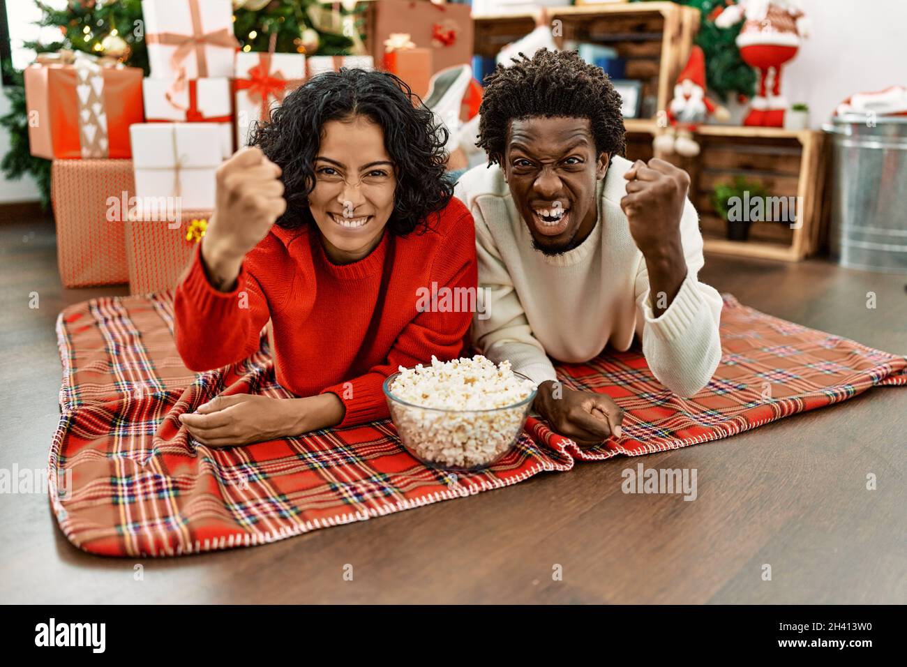 Young interracial couple lying by christmas tree annoyed and frustrated ...