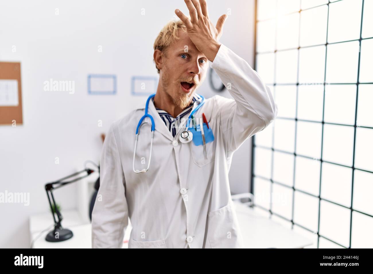 Young blond man wearing doctor uniform and stethoscope at clinic ...