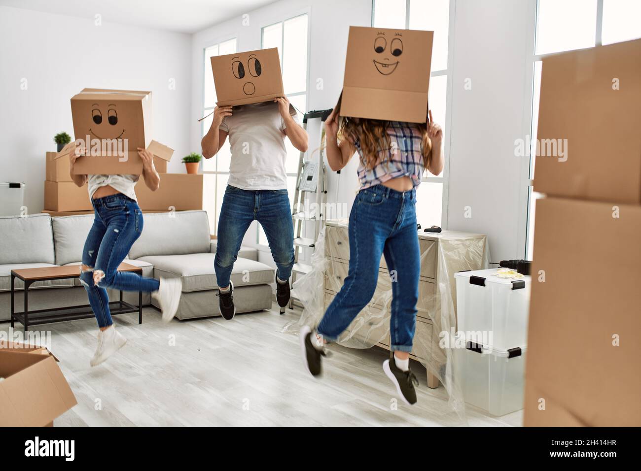 Mother and couple playing with funny cardboard box on head at home ...