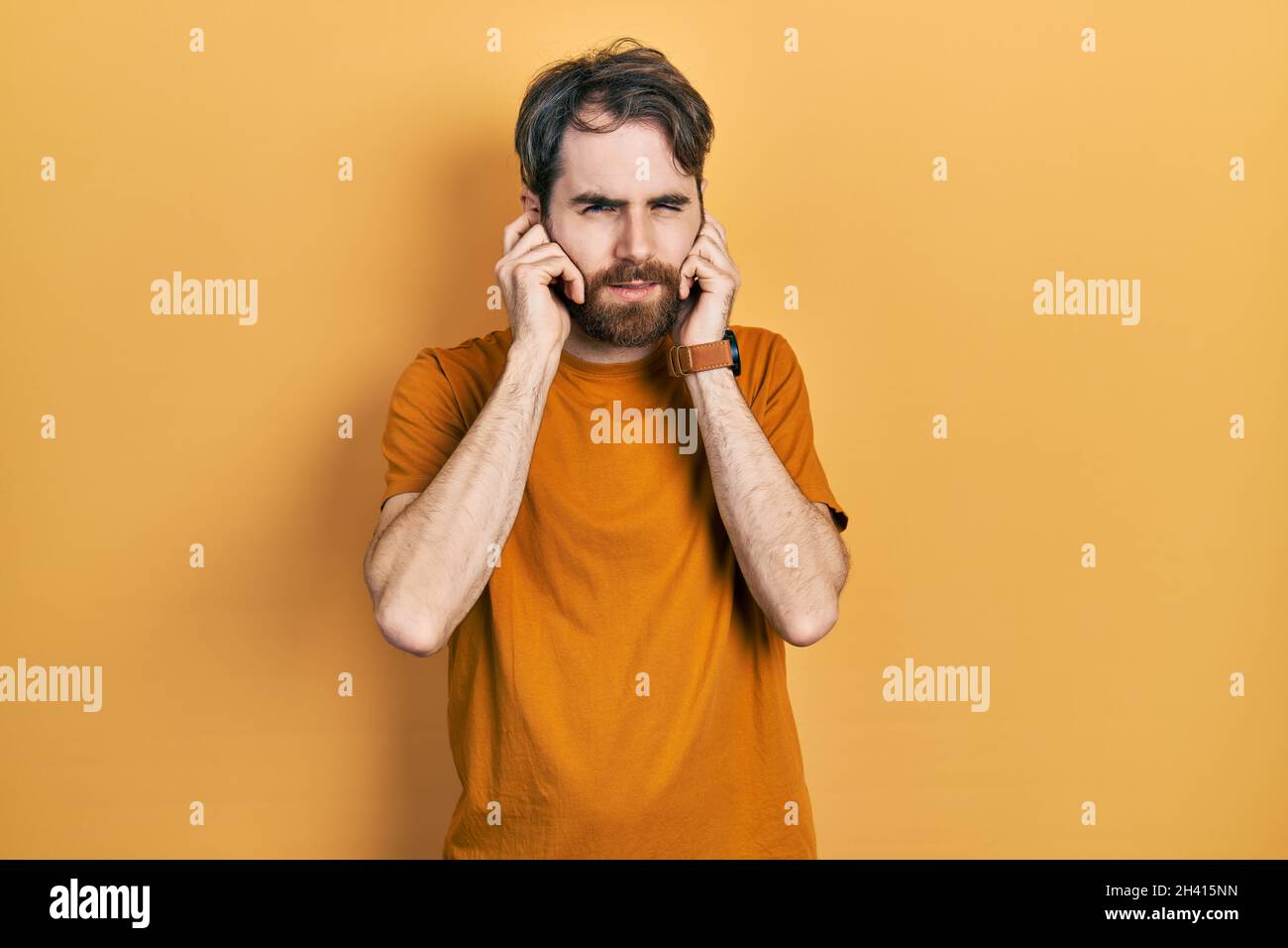 Caucasian man with beard wearing casual yellow t shirt covering ears ...