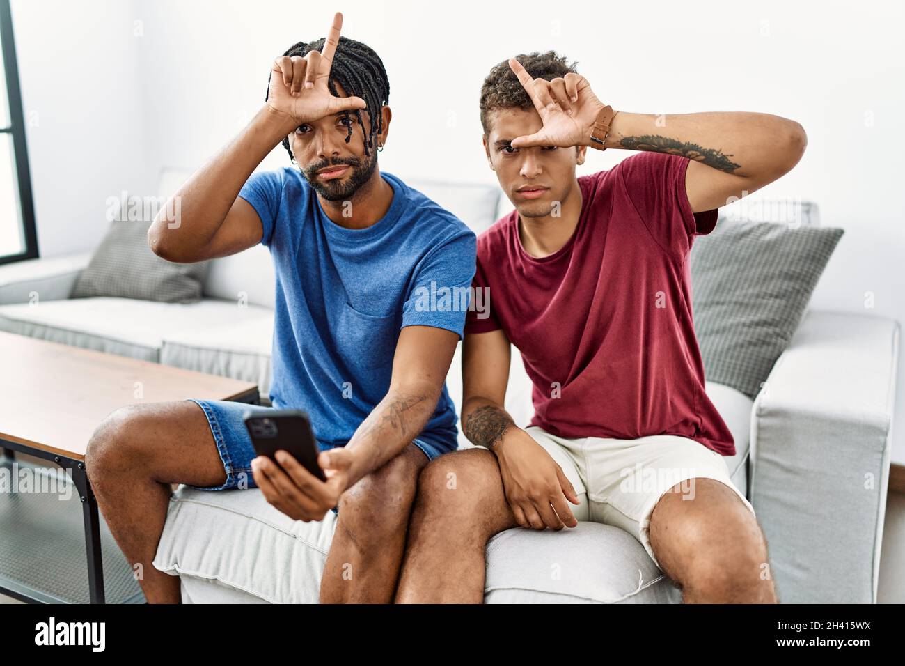 Young hispanic men using smartphone sitting on the sofa at home making ...
