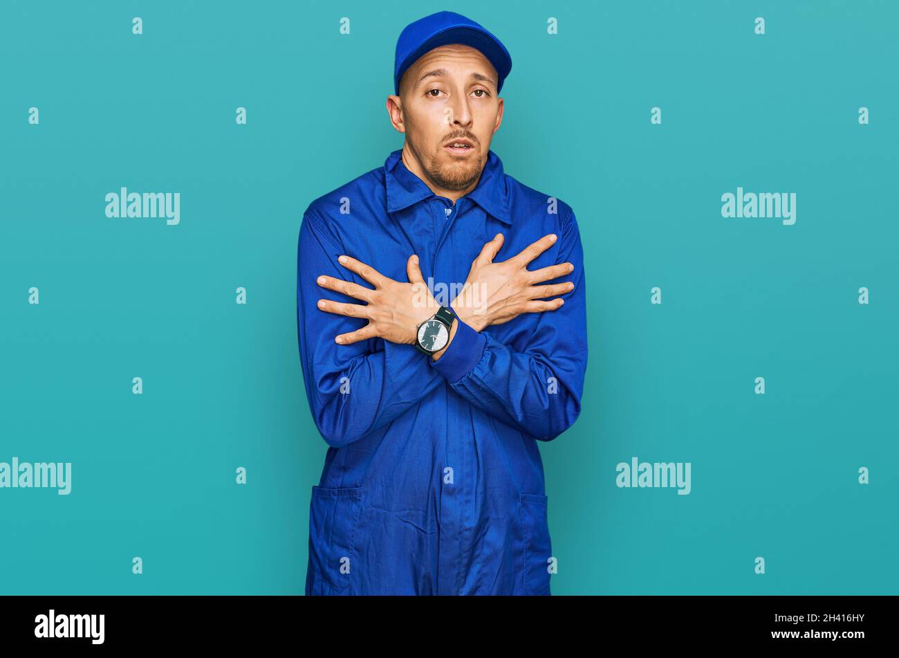 Bald man with beard wearing builder jumpsuit uniform shaking and ...