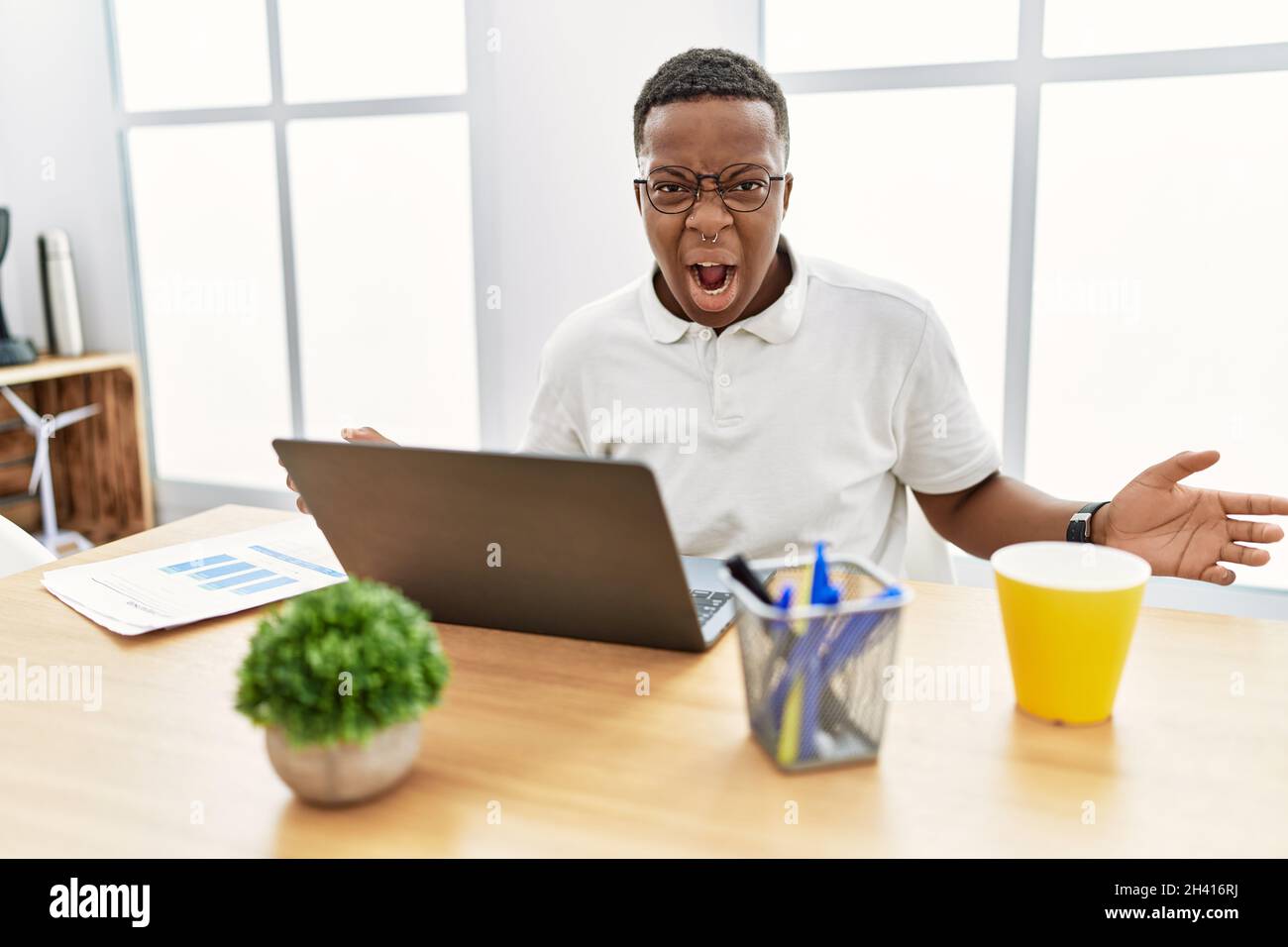 Young african man working at the office using computer laptop angry and ...