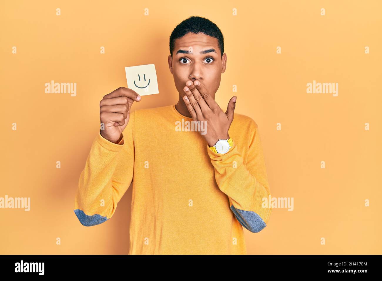 Young african american guy holding smile reminder covering mouth with ...