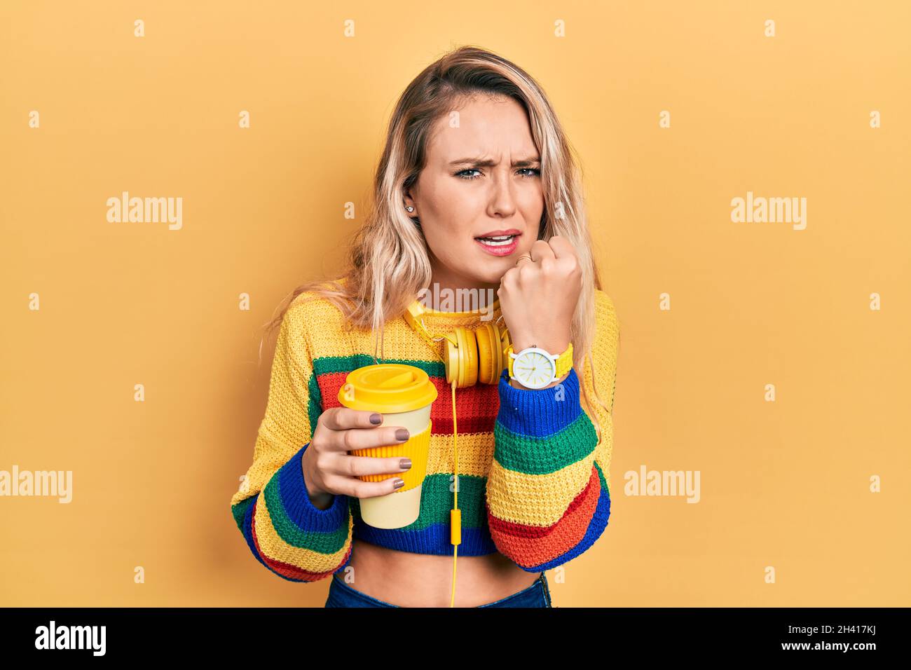 Beautiful young blonde woman drinking cup of coffee wearing headphones ...