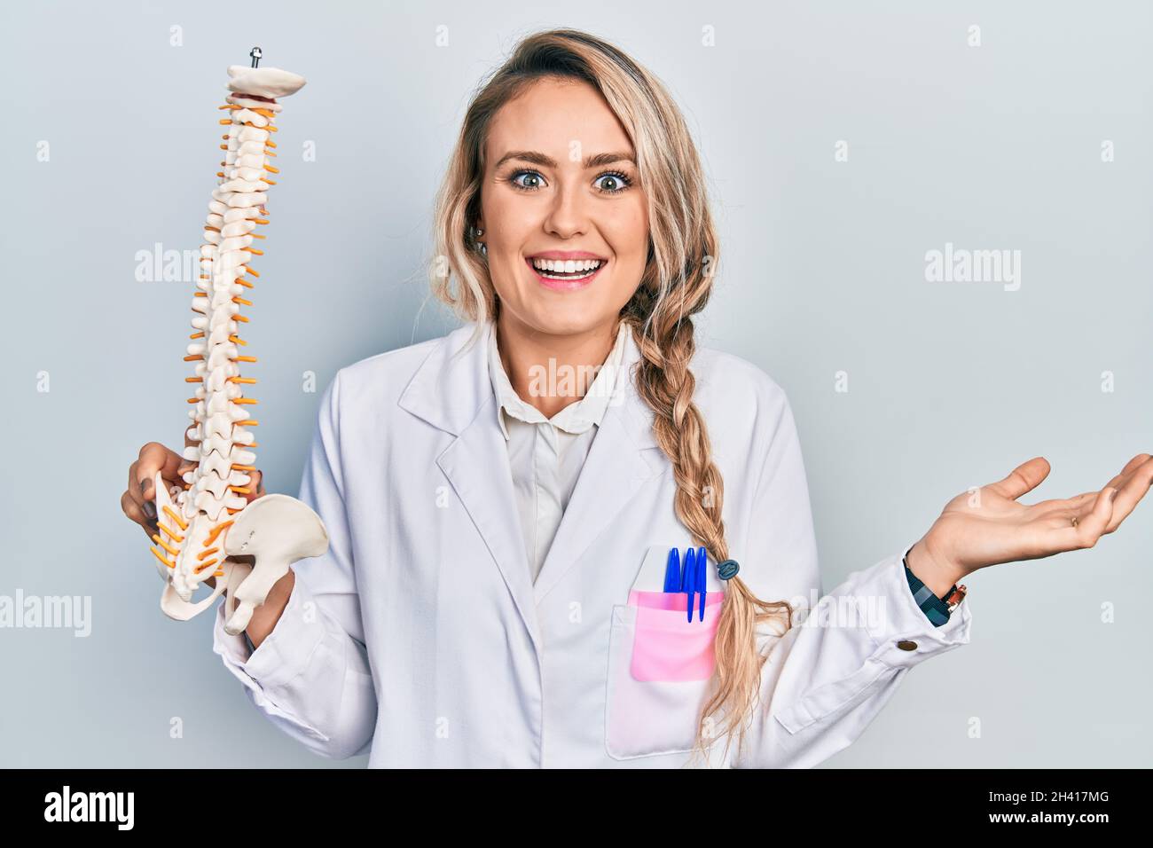 Beautiful young blonde doctor woman holding anatomical model of spinal ...