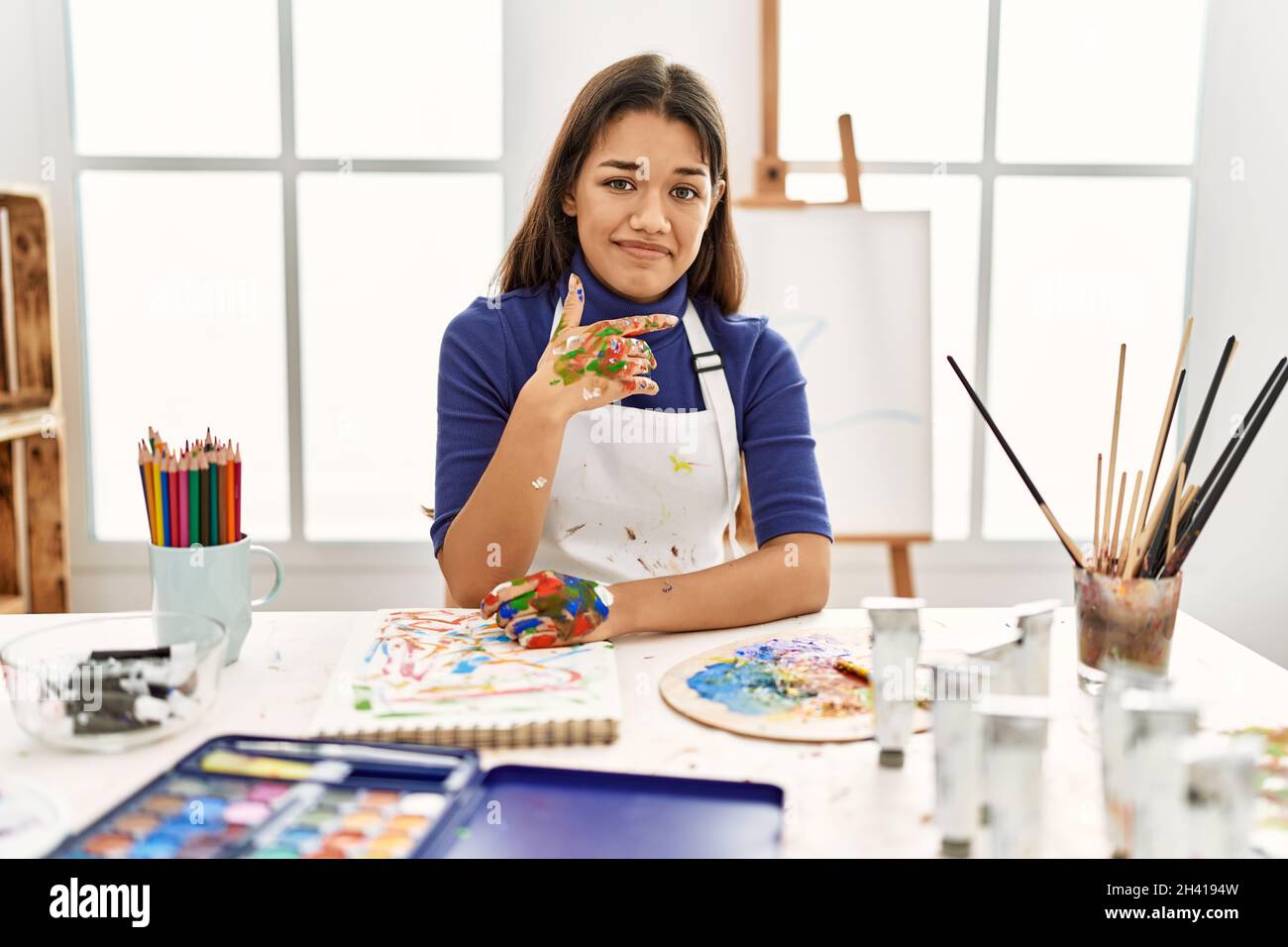 Young brunette woman at art studio with painted hands looking confident ...