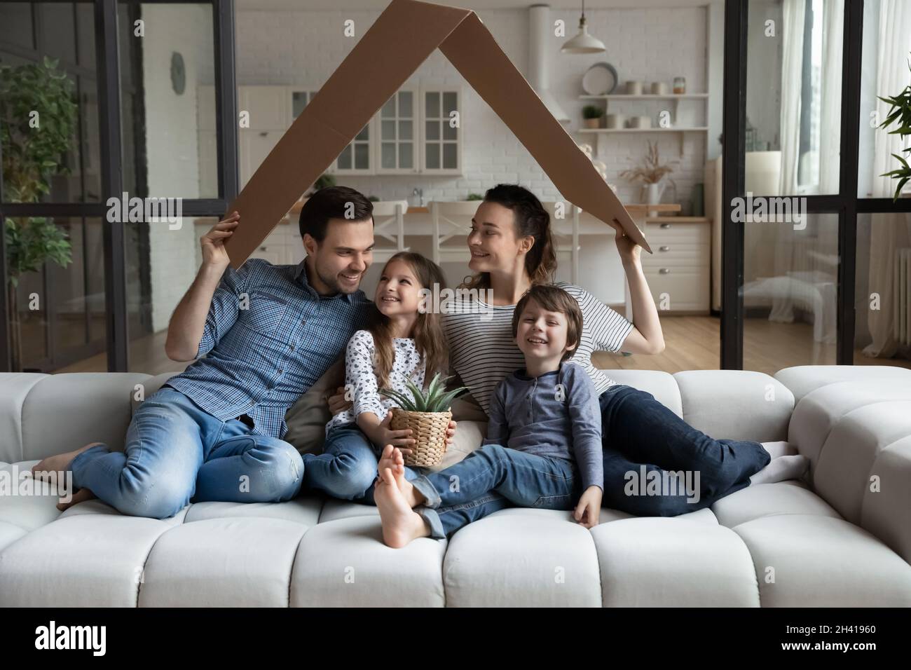 Happy bonding young parents sitting with kids under carton roof Stock ...